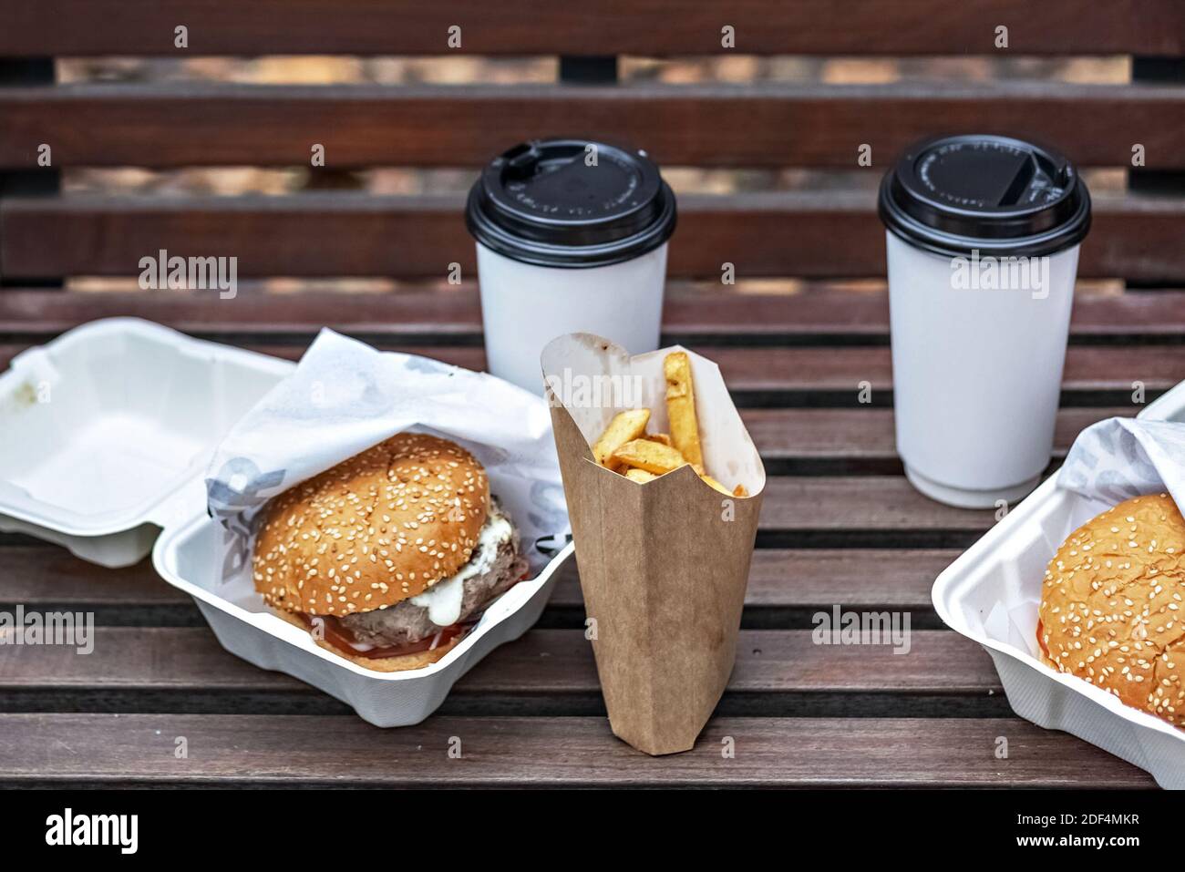 Fast food. Paper cups with coffee, hamburger boxes and fries on a park ...