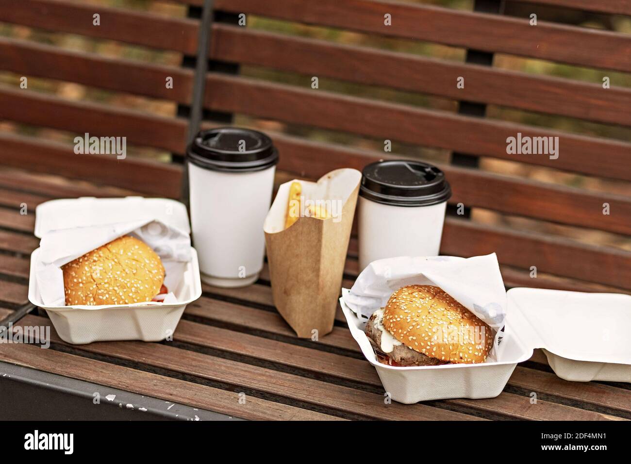 Fast food. Paper cups with coffee, hamburger boxes and fries on a park ...
