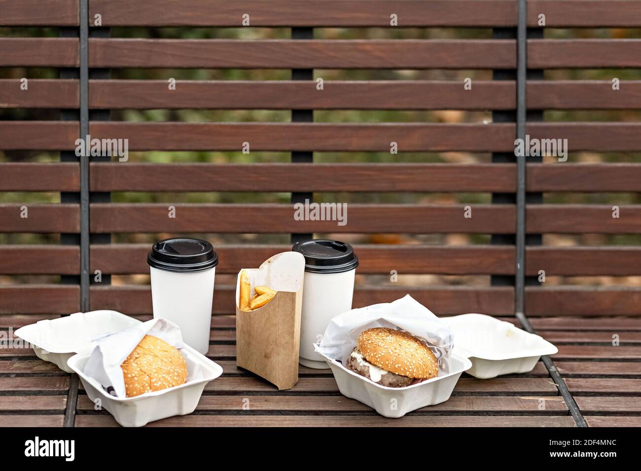 Fast food. Paper cups with coffee, hamburger boxes and fries on a park ...