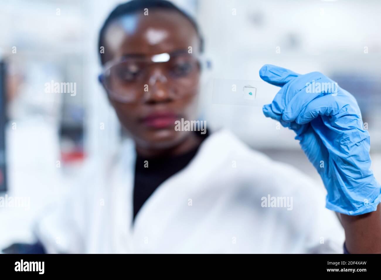 Sample glass slide in focus while chemist is looking at it during lab ...