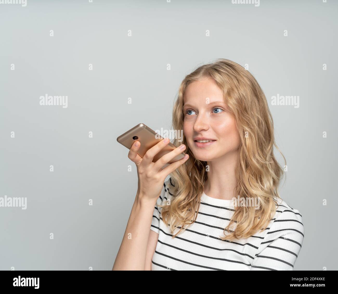 Pretty female dictating voice message on mobile phone standing near ...