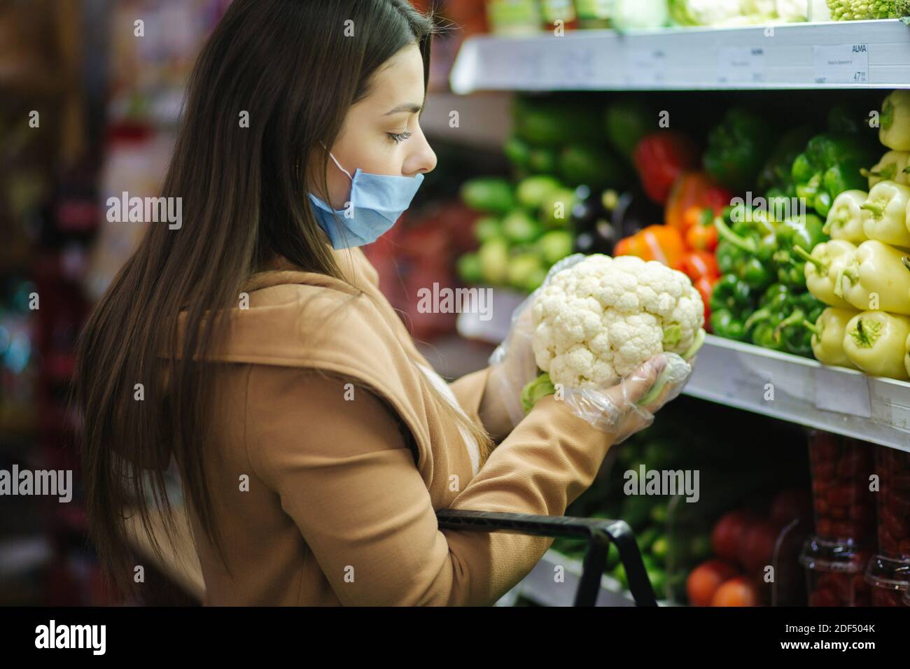 Happy woman in protective mask taking fresh vegetables while standing ...