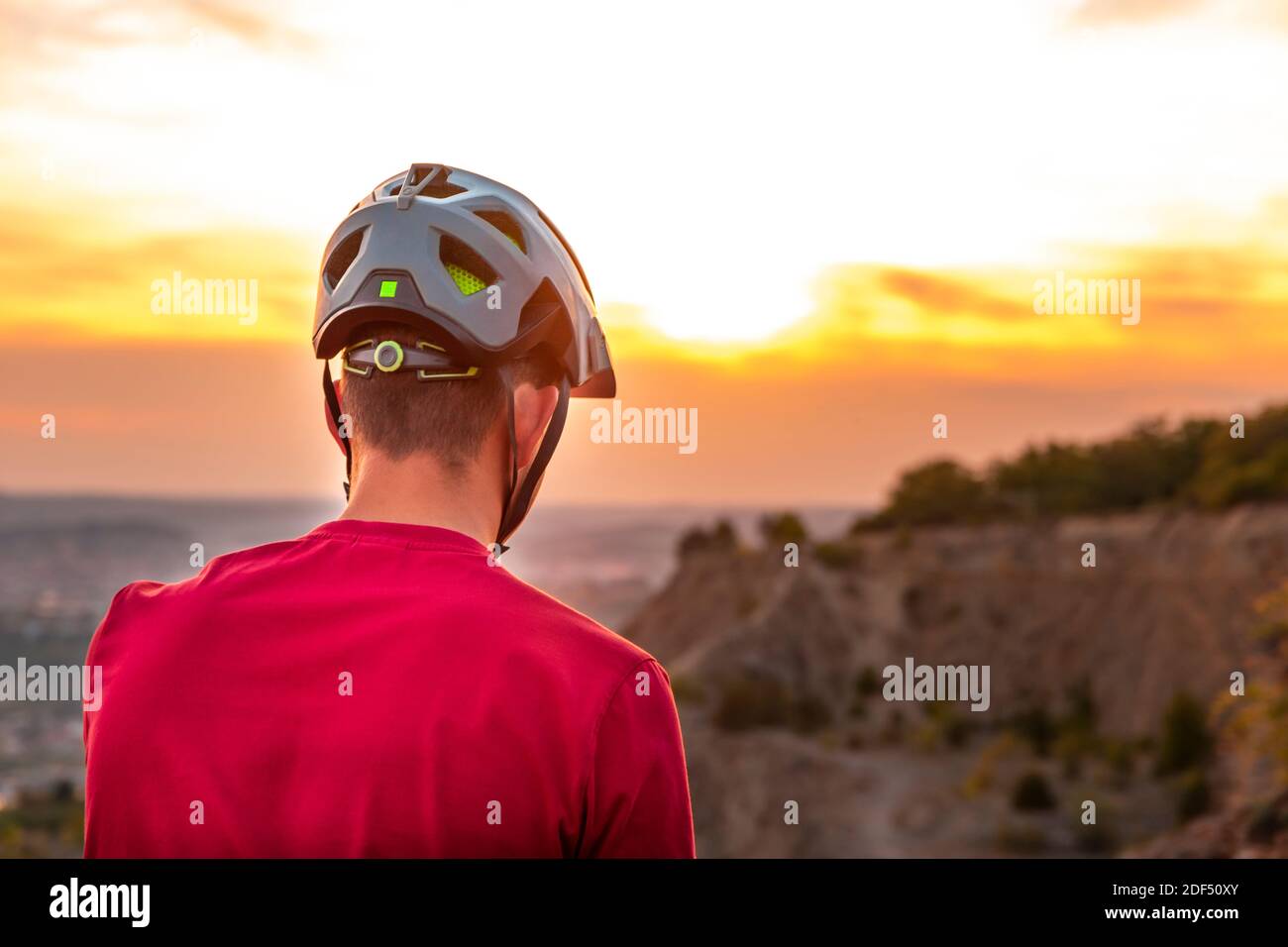 Back view of a man in a modern cycling helmet in the field at sunset ...