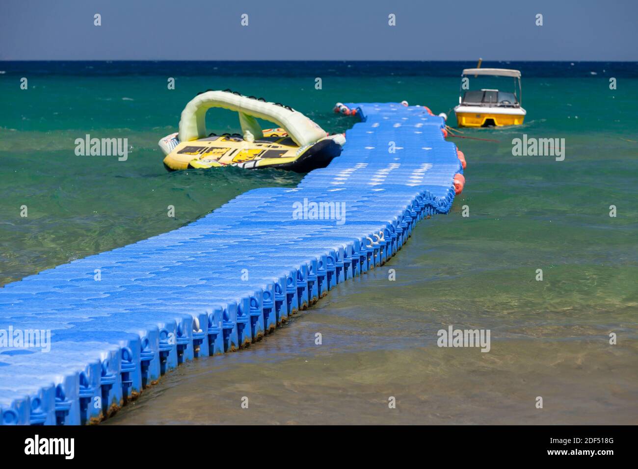 Blue plastic floating pier with moored motor boats. Beach at Greek ...