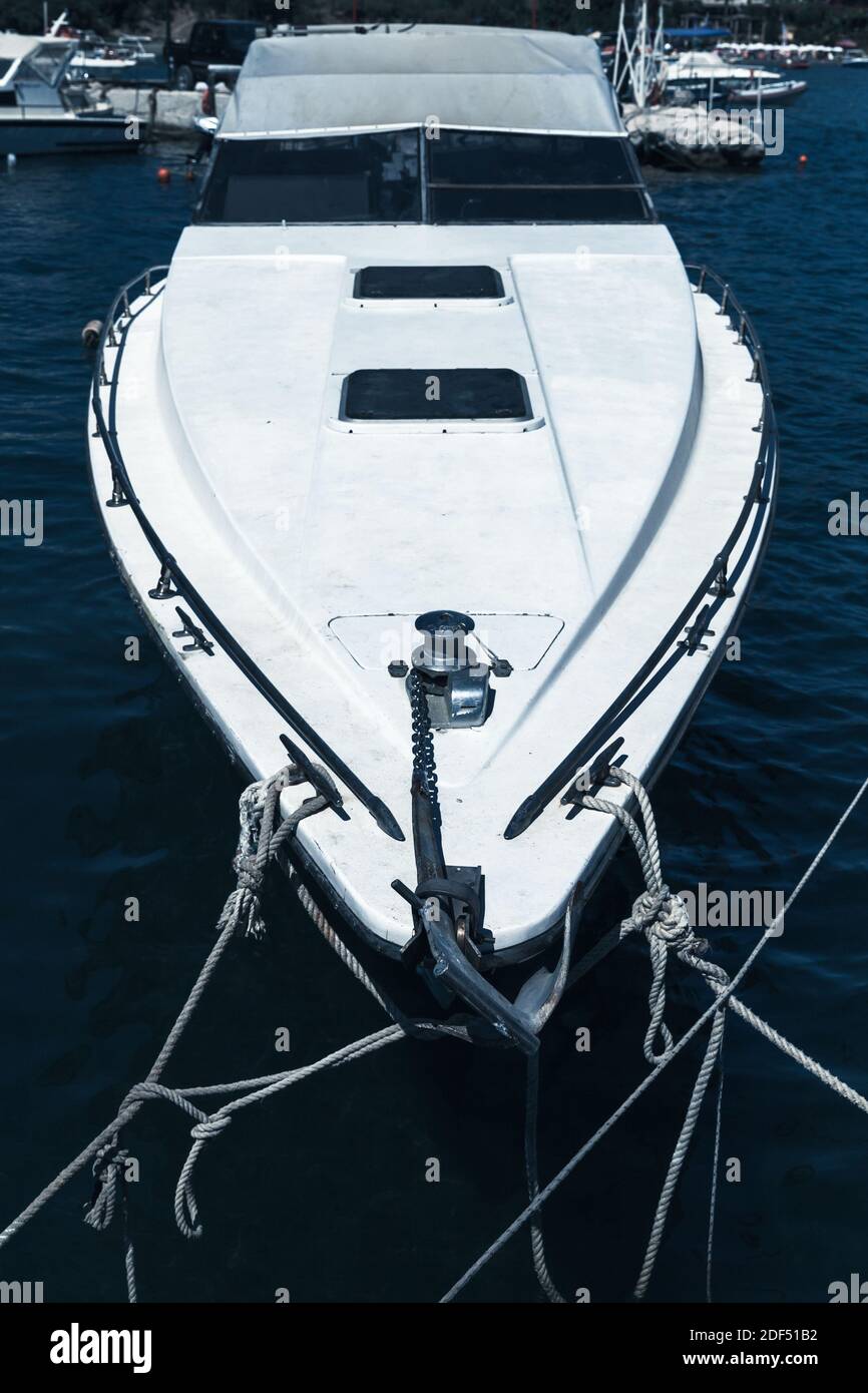 White yacht moored in port, bow and ropes close-up. Blue toned vertical ...