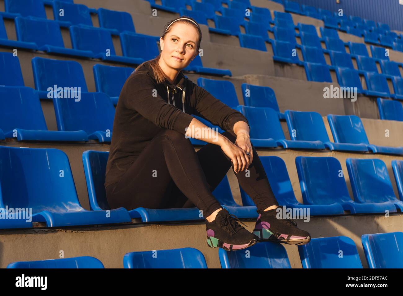 Fitness woman in black tracksuit sitting on the podium of the stadium ...