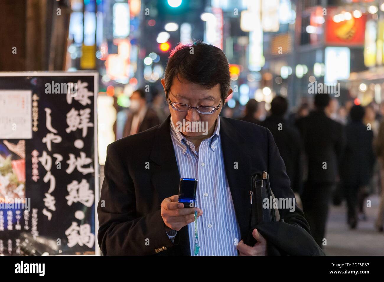 A salaryman or Japanese male office worker checks his mobile telephone ...