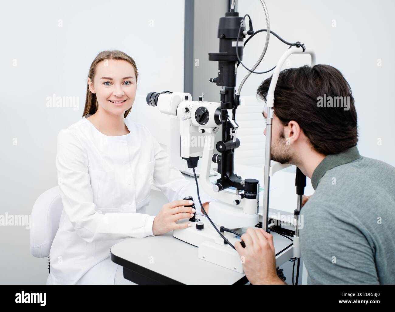Optometrist woman looking at camera during eye examination of a male ...