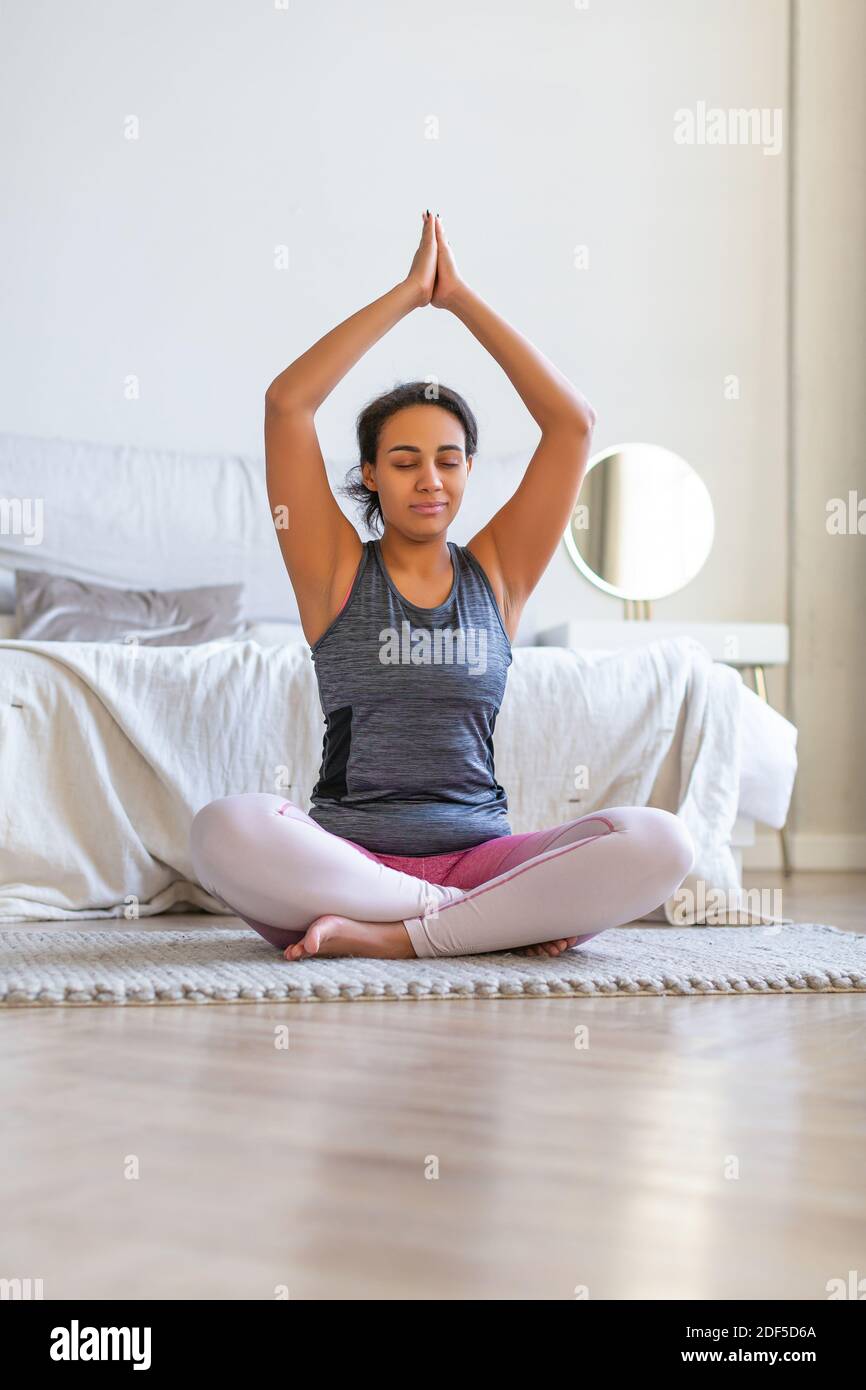 Yoga practice at home. African American woman meditating while doing ...