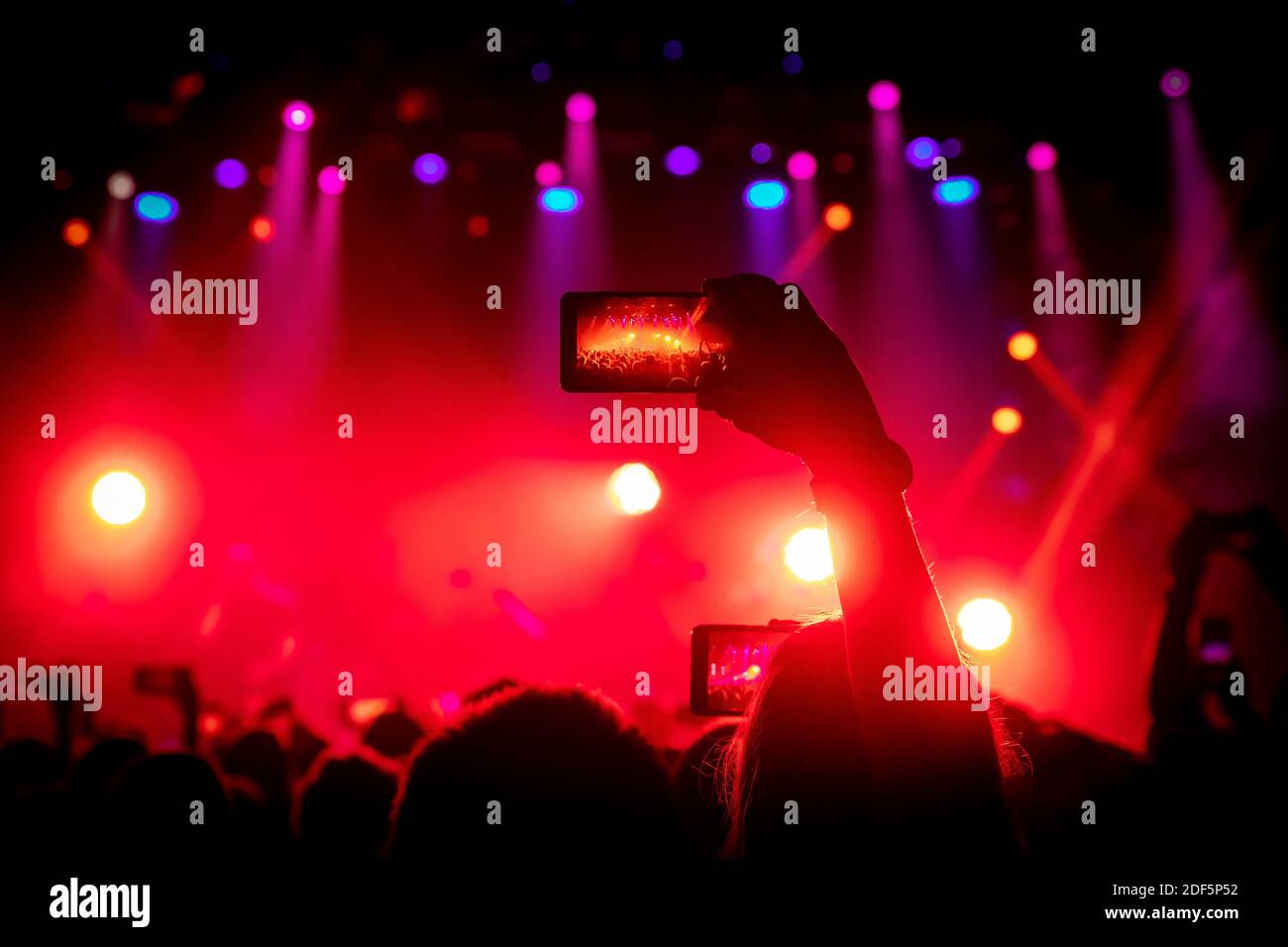 Smartphone in hand at a concert, red light from stage Stock Photo - Alamy
