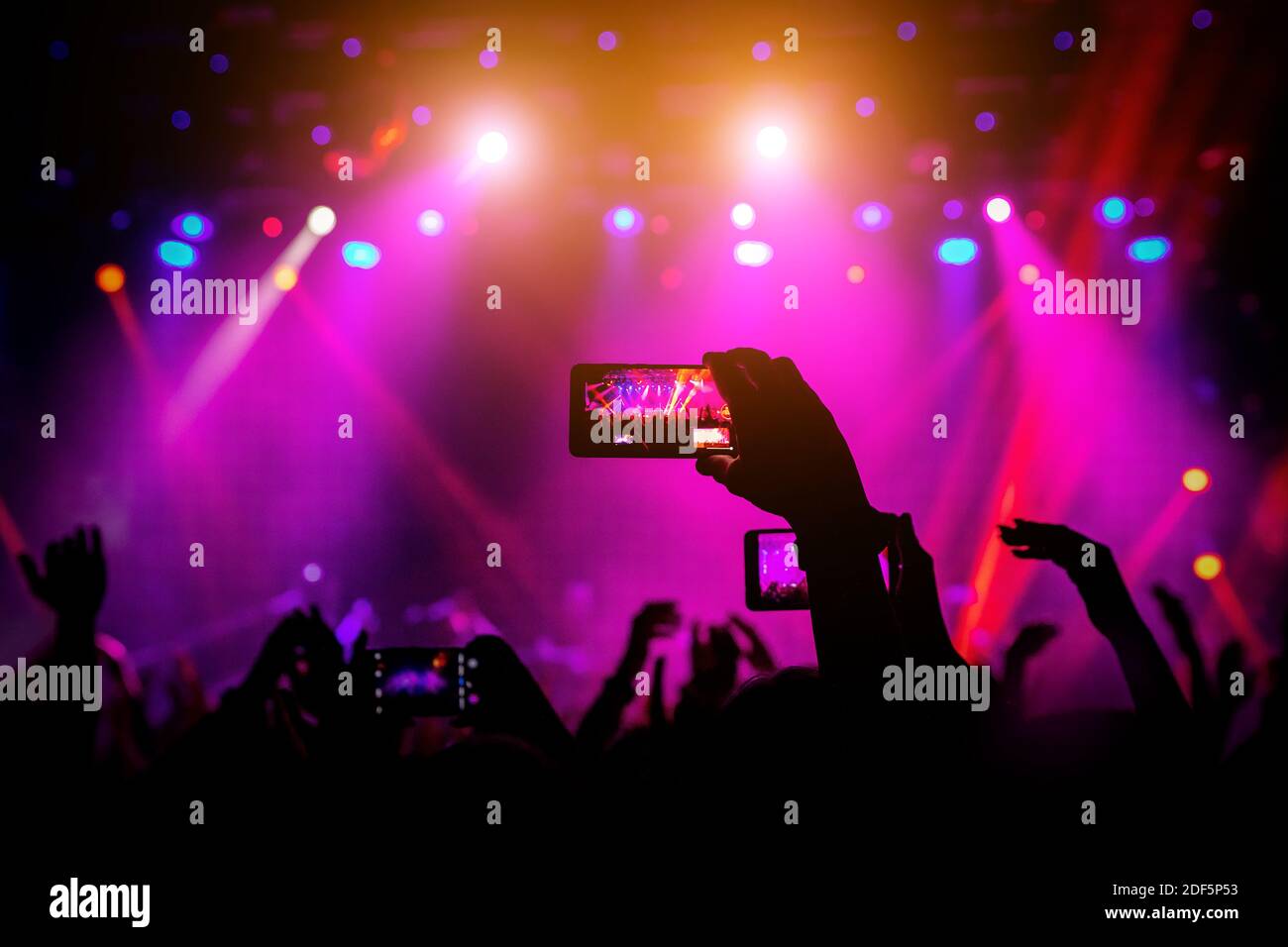 Smartphone in hand at a concert, red light from stage Stock Photo - Alamy