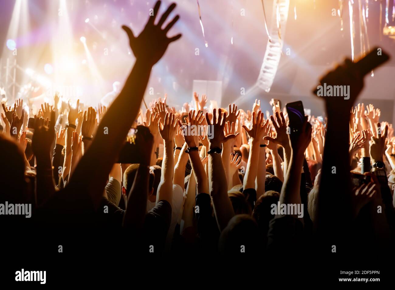 A man with his hands up at a concert of his favorite group. Light from ...