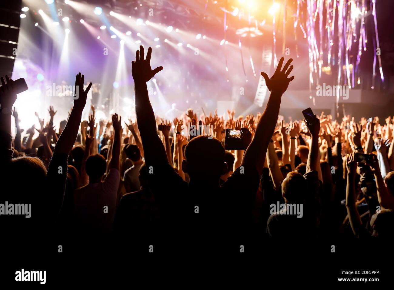 A man with his hands up at a concert of his favorite group. Light from ...