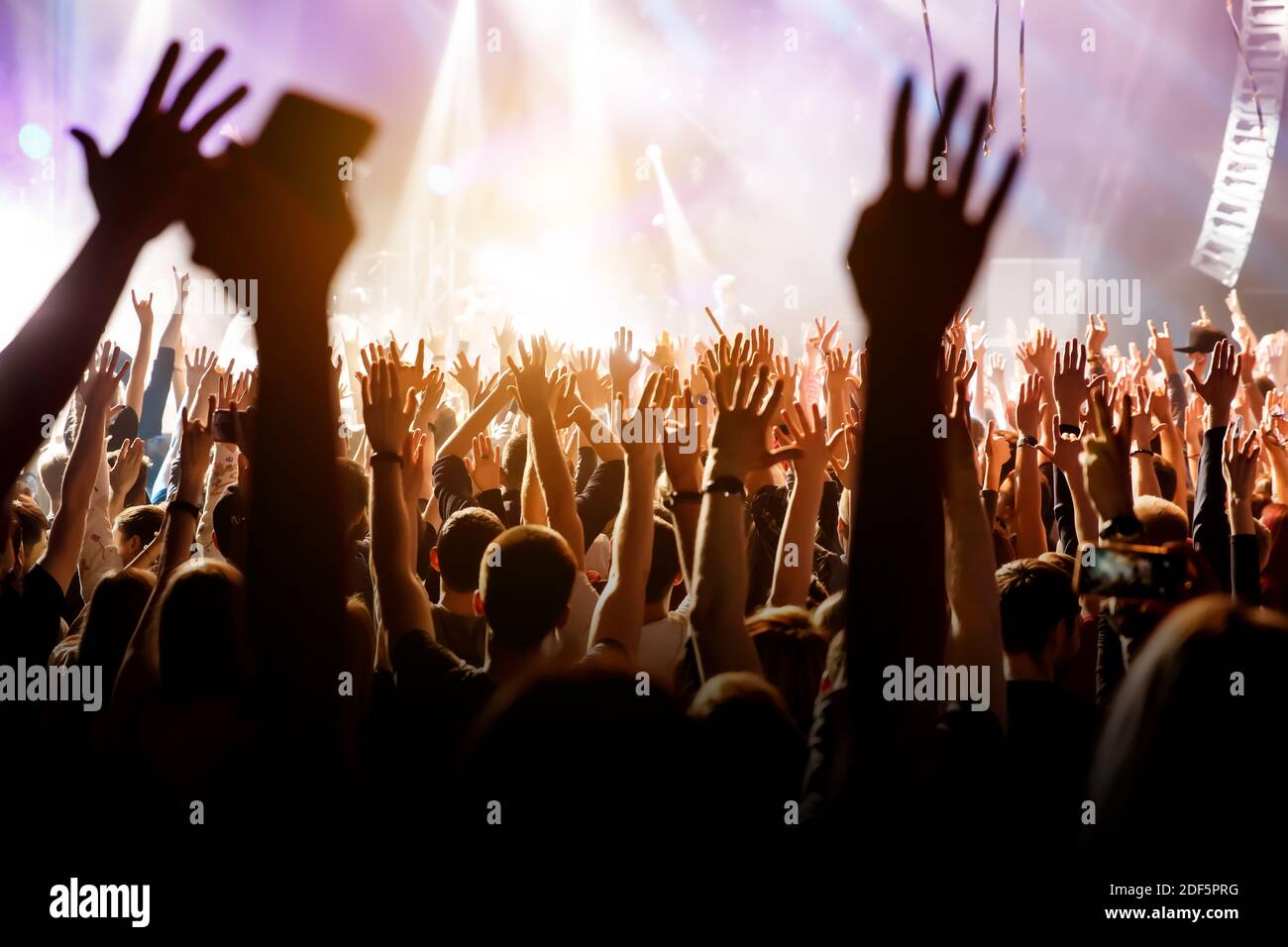 A man with his hands up at a concert of his favorite group. Light from ...