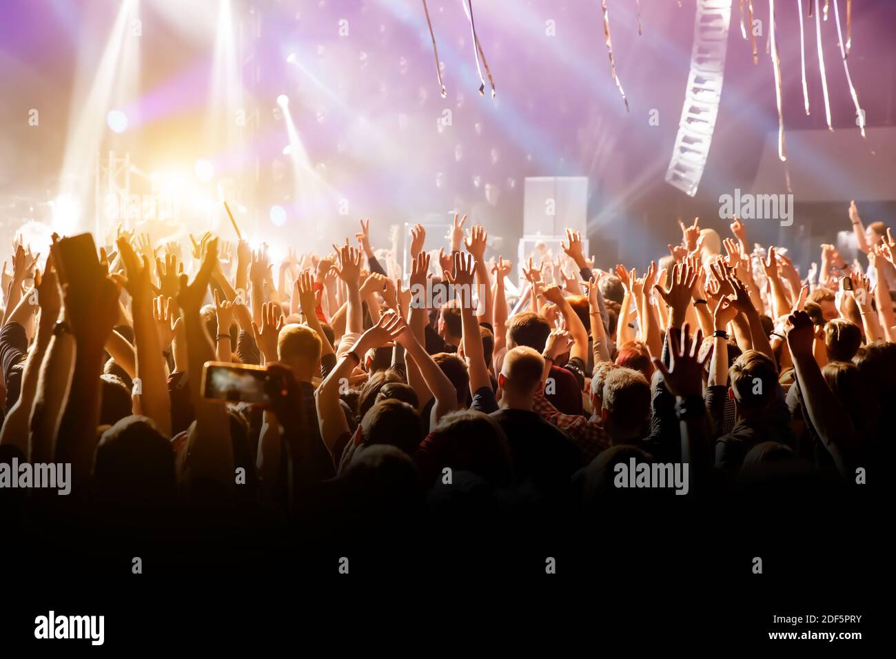 A man with his hands up at a concert of his favorite group. Light from ...