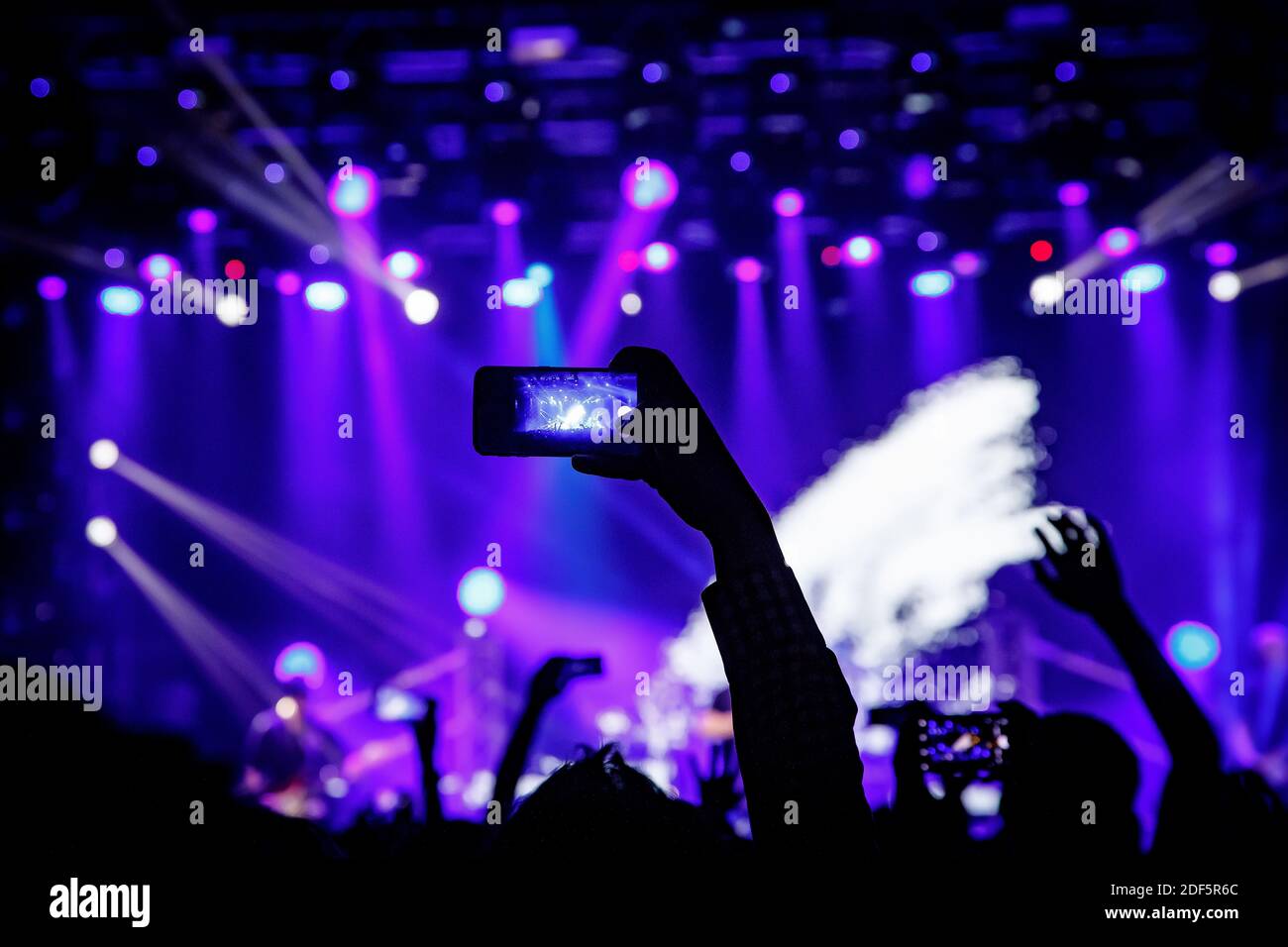 Smartphone in hand at a concert, blue light from stage Stock Photo - Alamy