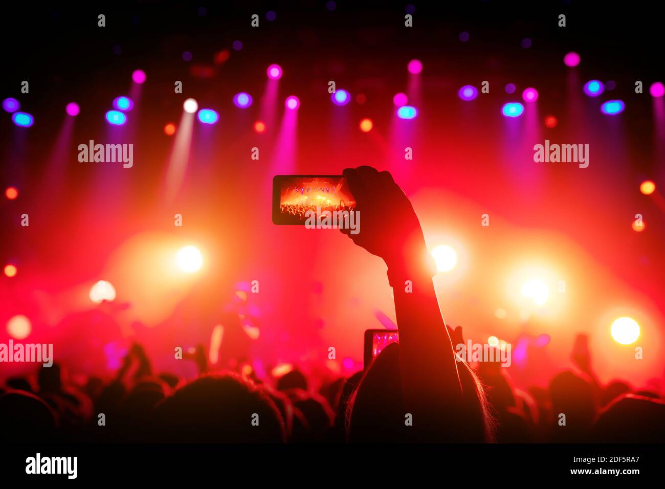 Smartphone in hand at a concert, red light from stage Stock Photo - Alamy