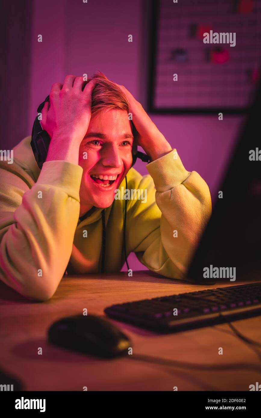 Cheerful gamer in headset looking at computer monitor near keyboard on ...