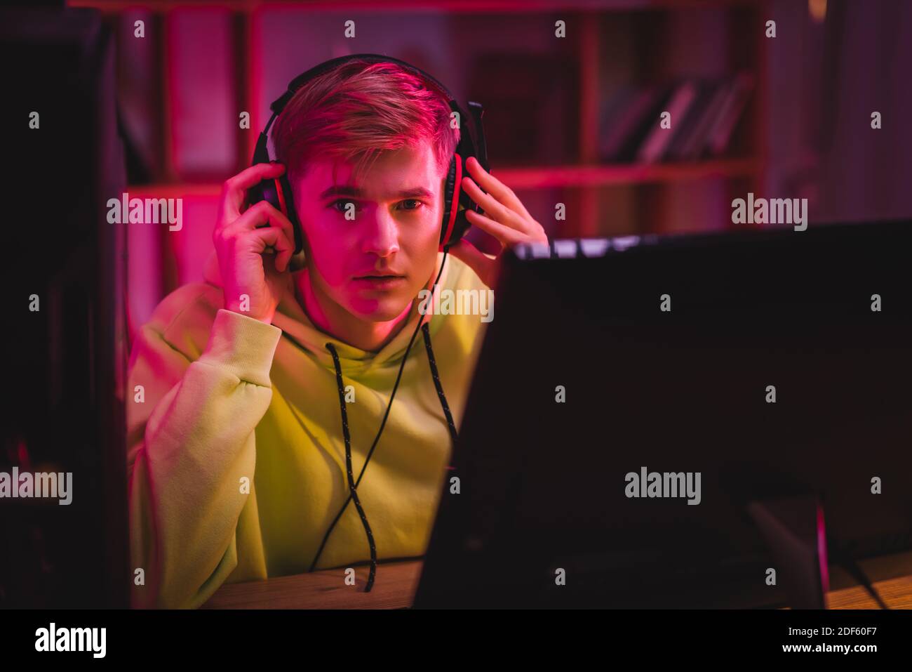 Young gamer holding headphones and looking at camera near computer ...