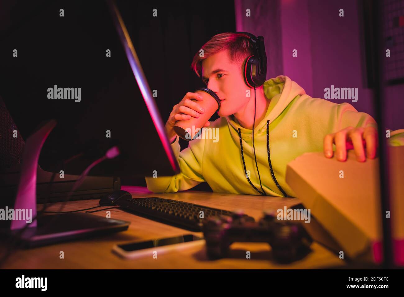 Young gamer in headphones drinking coffee to go and holding pizza box ...