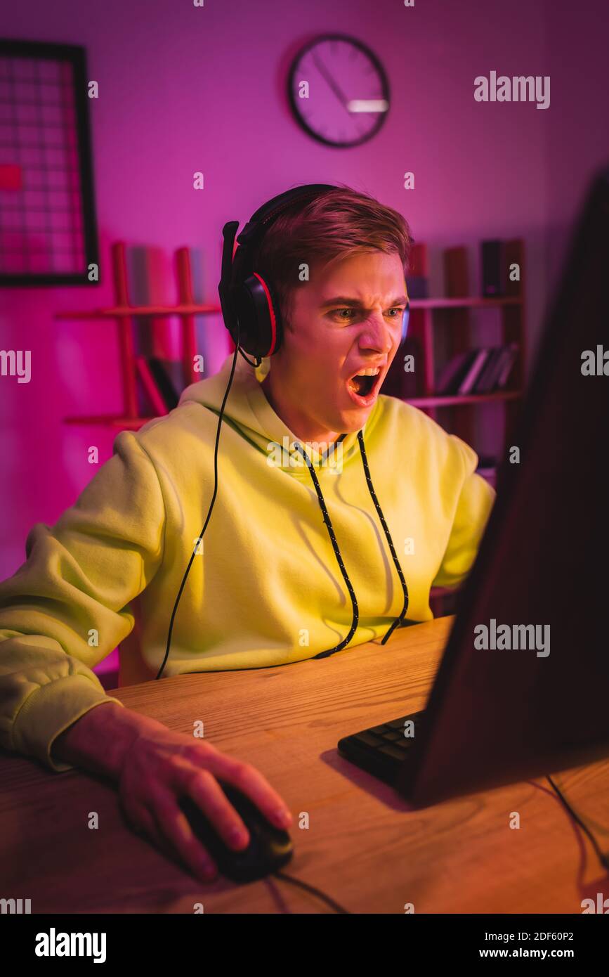 Aggressive gamer using computer on blurred foreground on table Stock ...