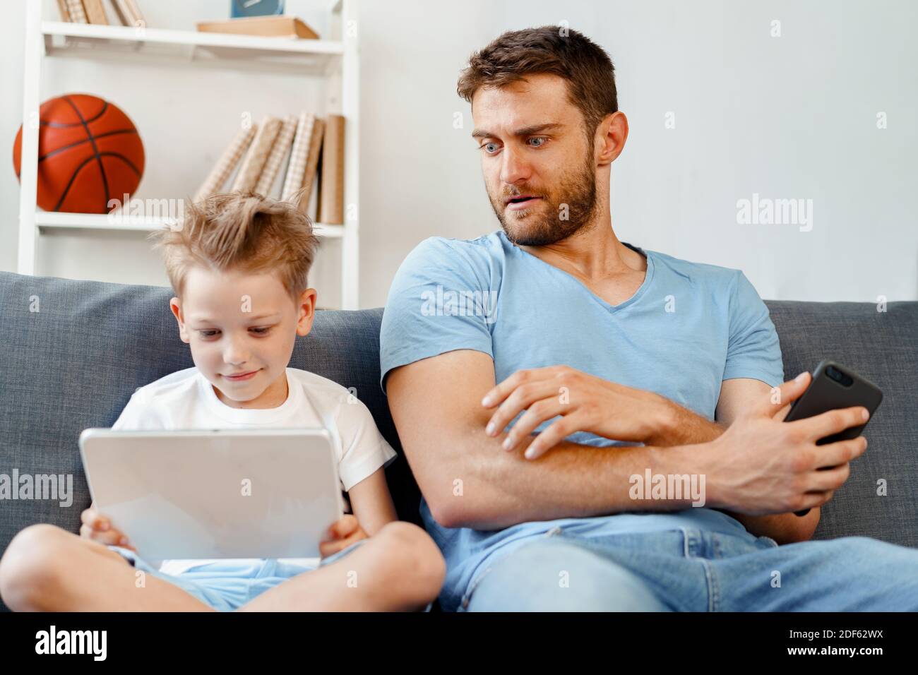 Worried father peeking at what his son is watching on digital tablet ...