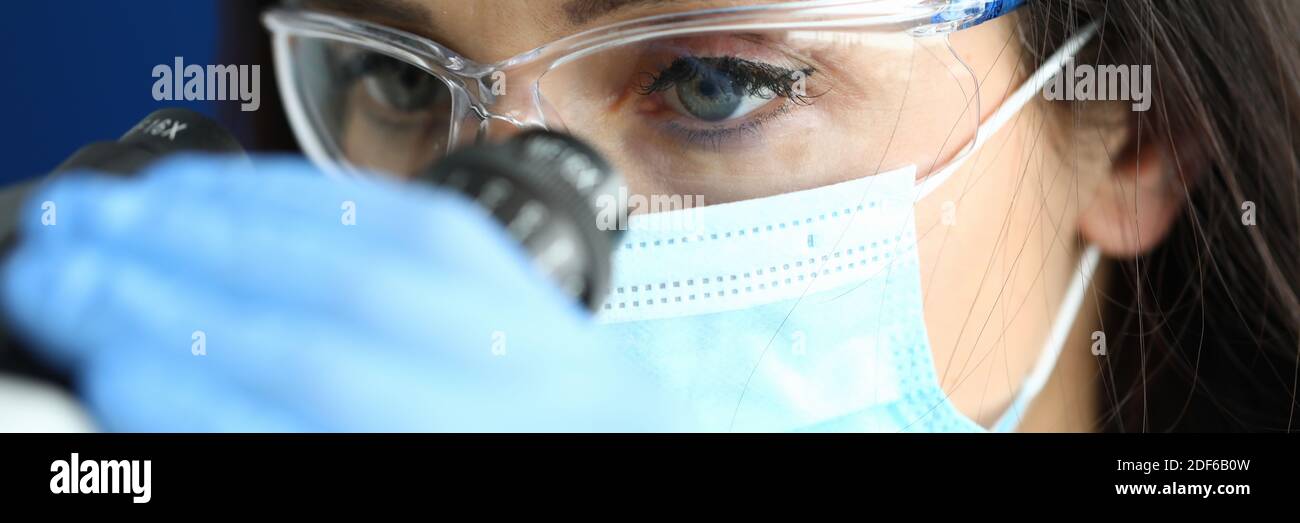 Portrait of woman in mask and glasses looks through microscope Stock ...