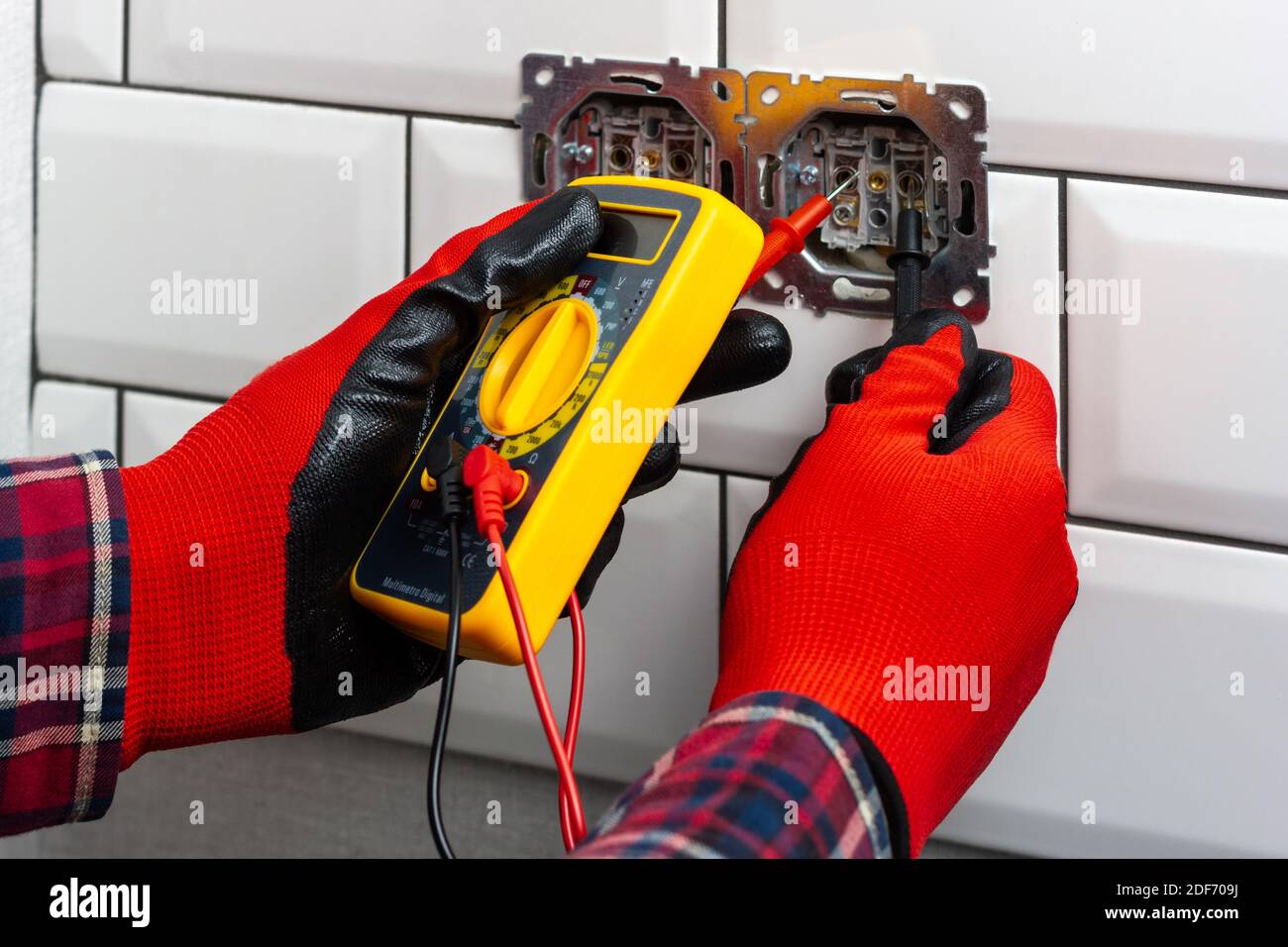 A guy in red work gloves, using a multimeter - tester, measures the ...