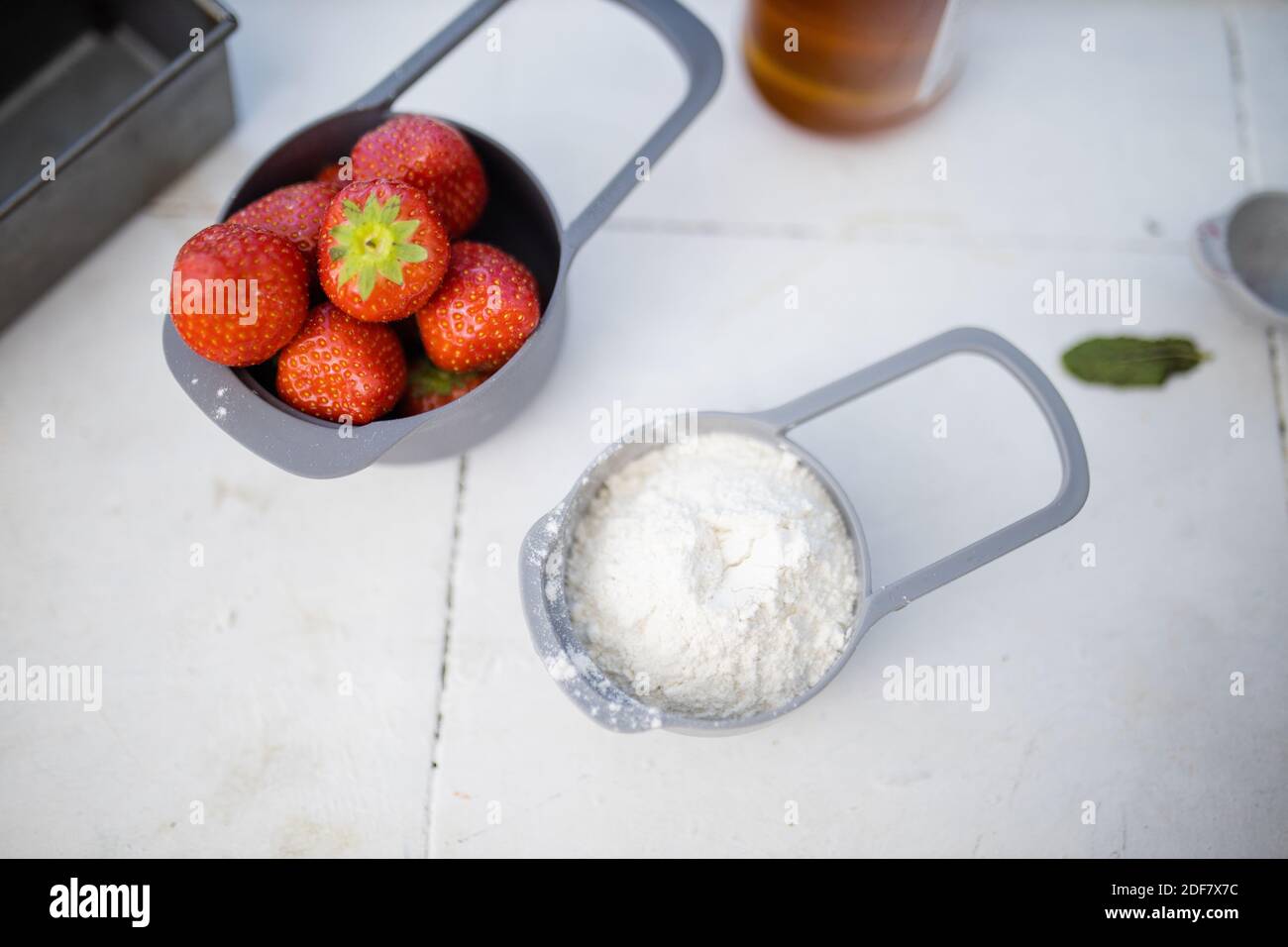 Strawberries and flour in measuring cups above white counter Stock ...