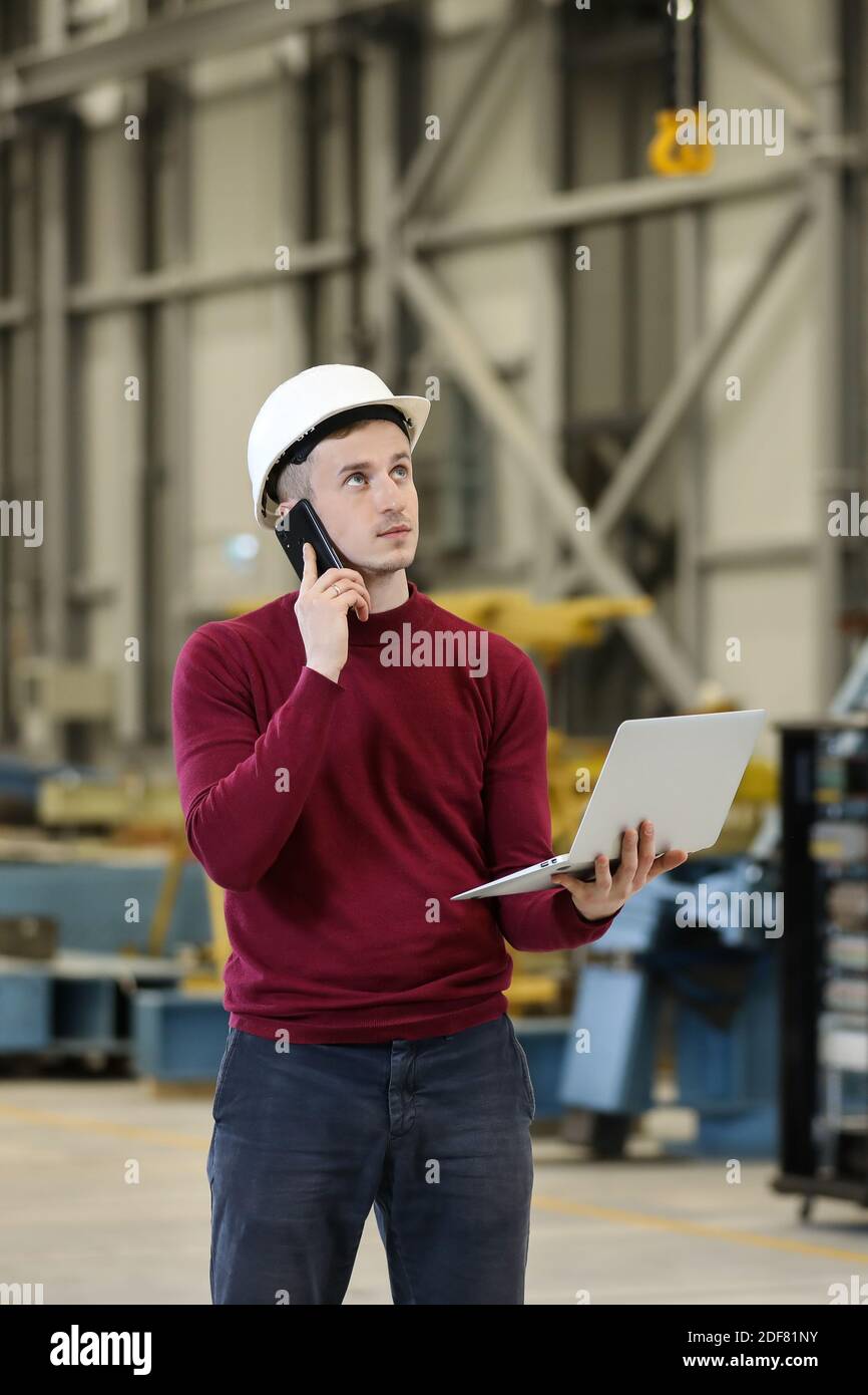 Portrait of a male factory manager in a white hard hat and red sweater ...