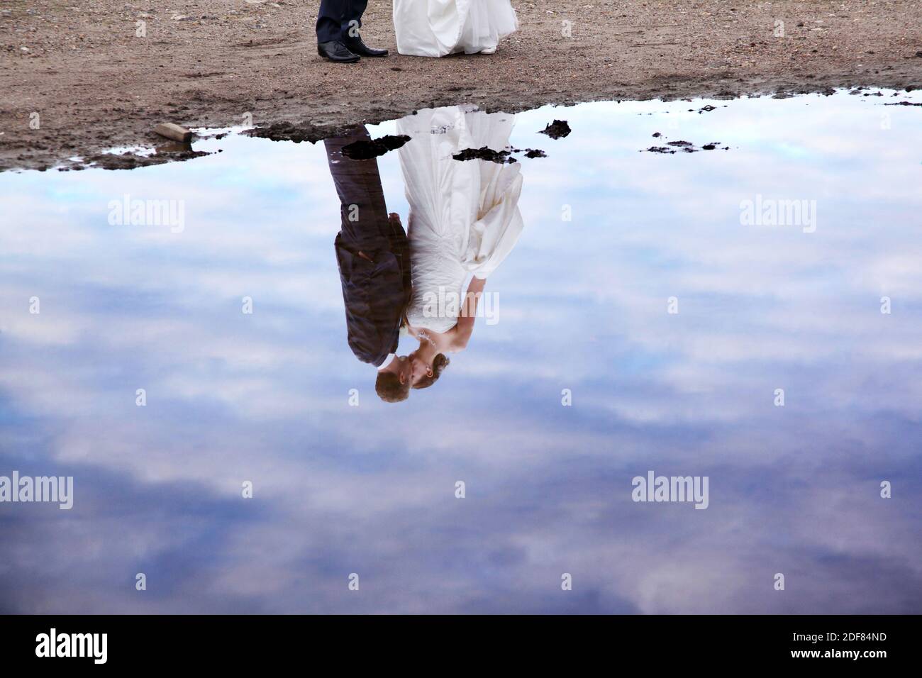 Kissing bride and groom couple reflected in water on their wedding day ...