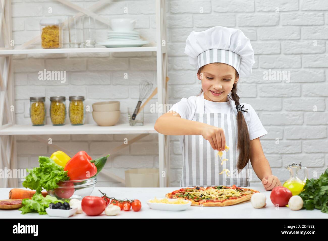 little girl in chef hat and an apron cooking pizza in the kitchen ...