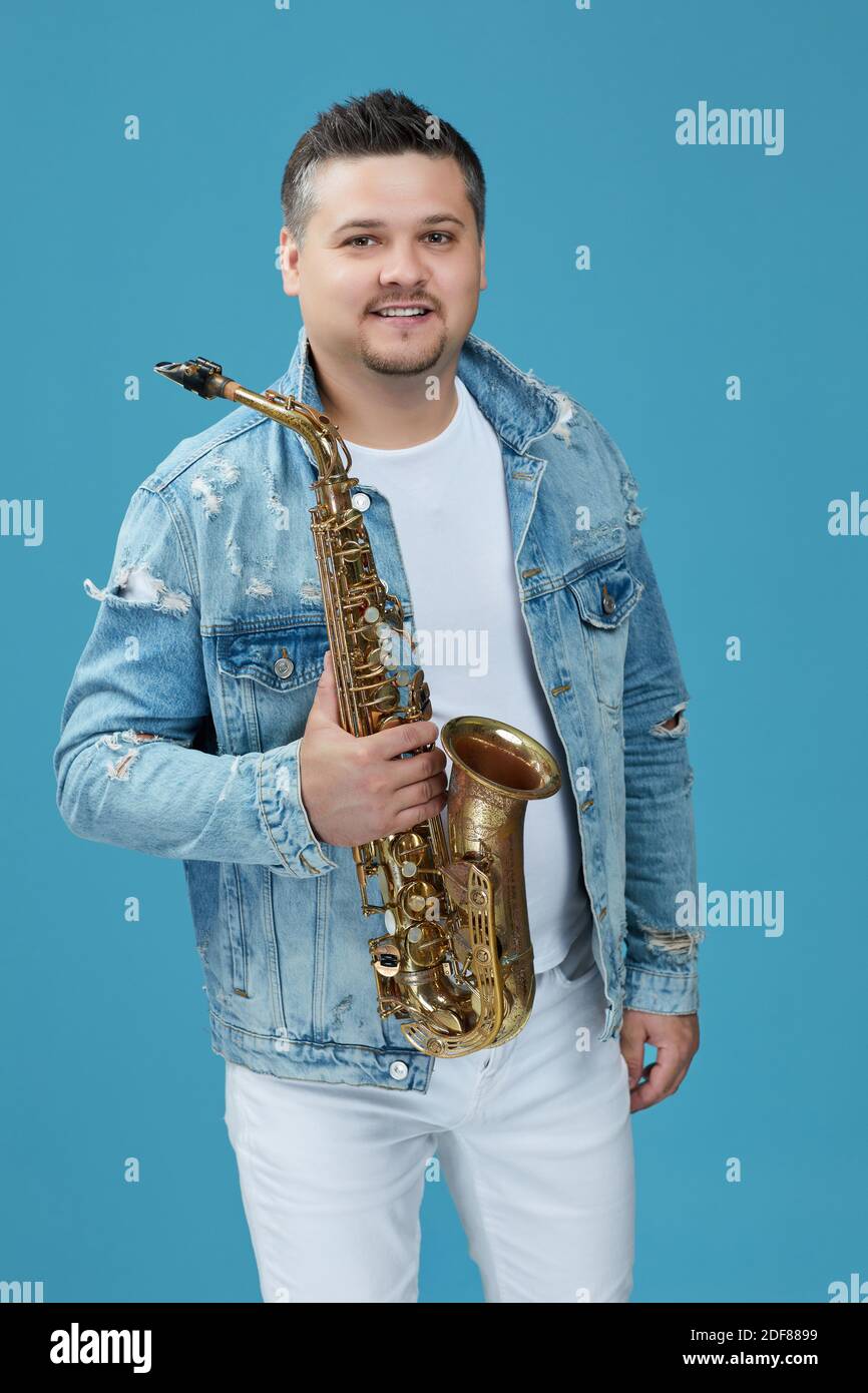 happy musician man with the saxophone on blue studio background. Music ...