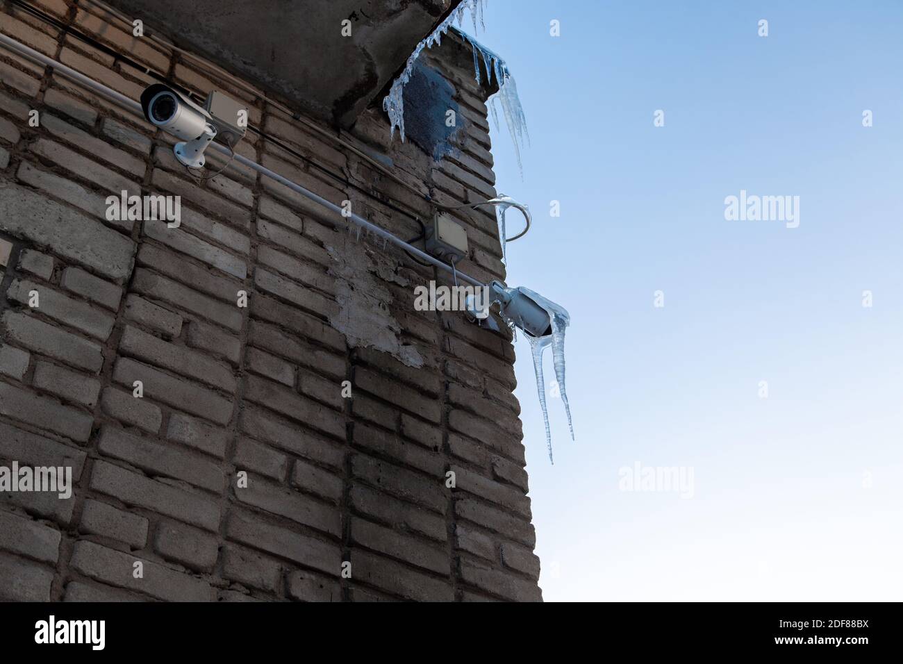 Two street surveillance cameras attached to a brick wall are heavily ...