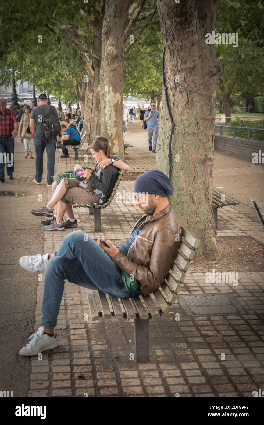 A young man wearing a brown leather jacket engaged on his mobile phone ...