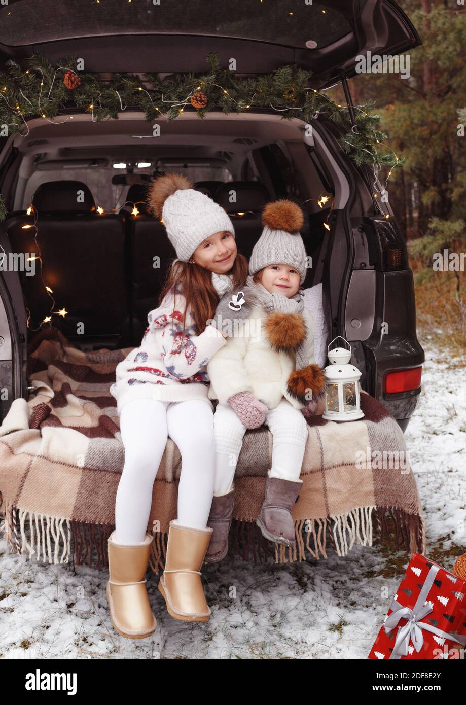 two teenage girls hug in the trunk of a car decorated with Christmas ...