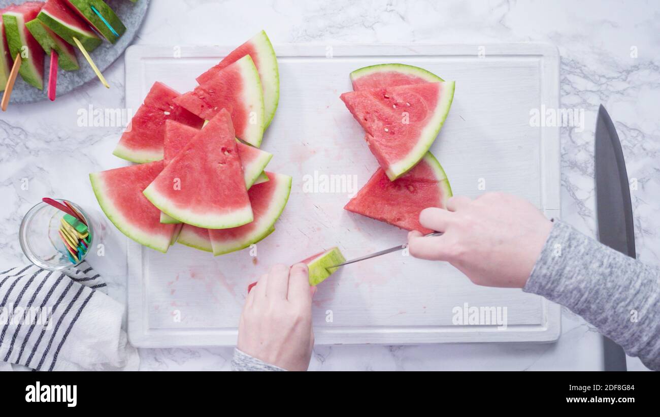 Flat lay. Slicing red watermelon into small pieces on a white cutting ...