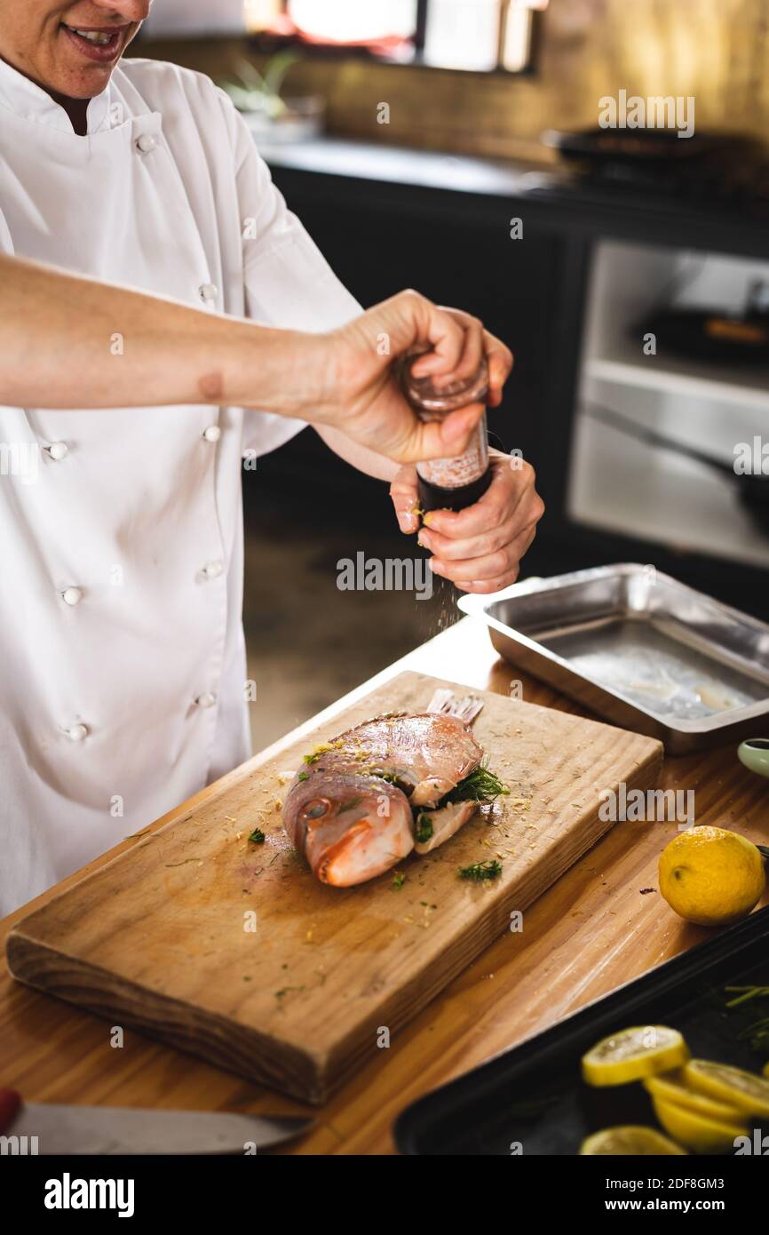 Mid section of chef grinding pepper over roasted fish in restaurant ...