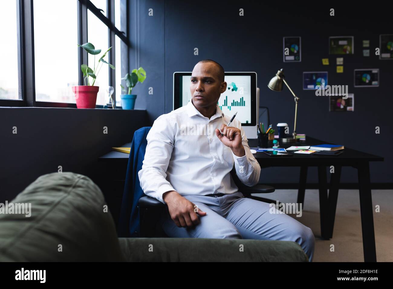 Mixed race businessman sitting by desk in office, thinking Stock Photo ...