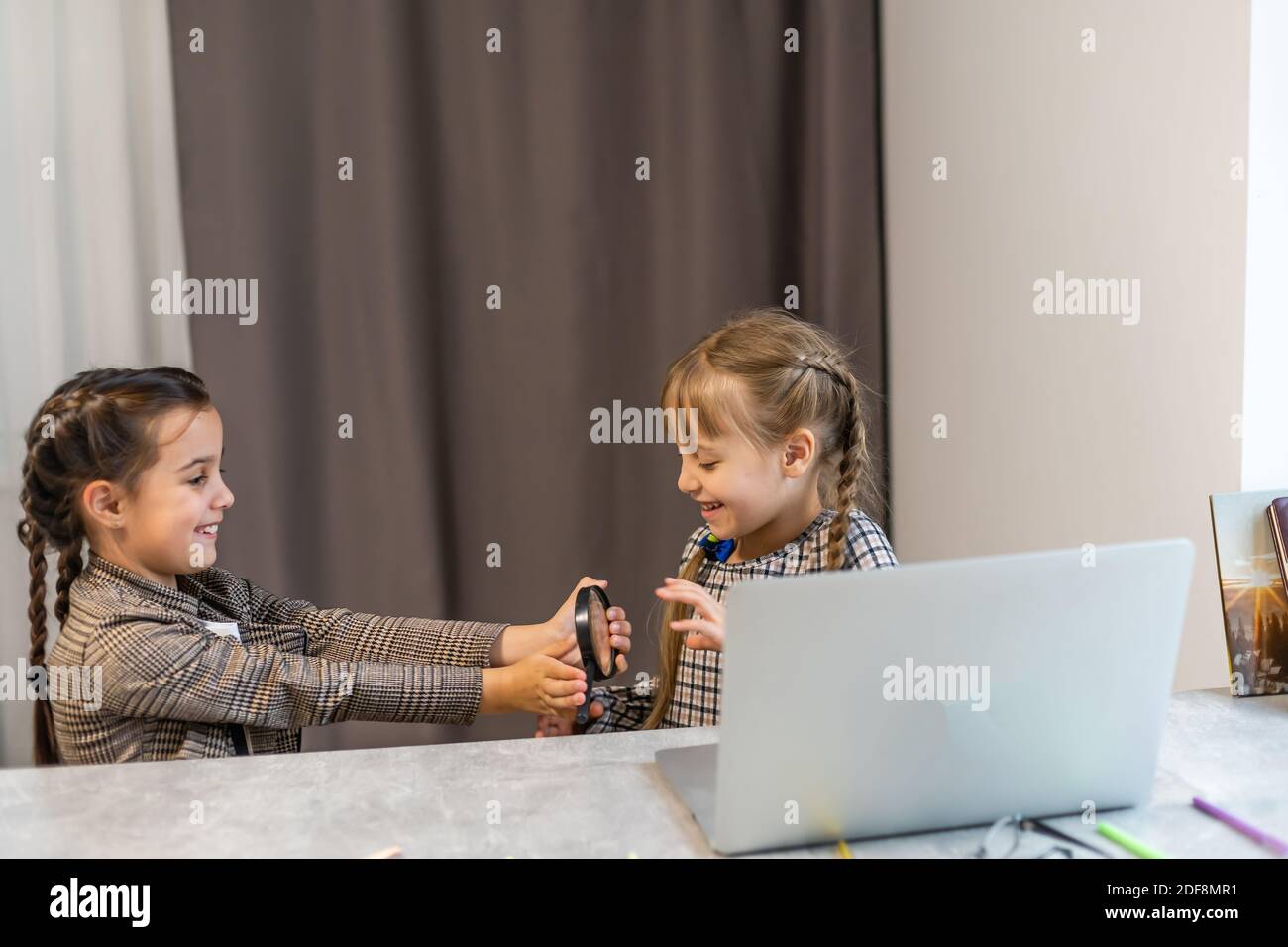Education at home concept - two Cute little playful girls studying doing homework on laptop ...