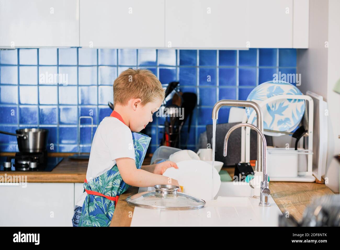 a boy in an apron washes dishes in the kitchen at home Stock Photo - Alamy