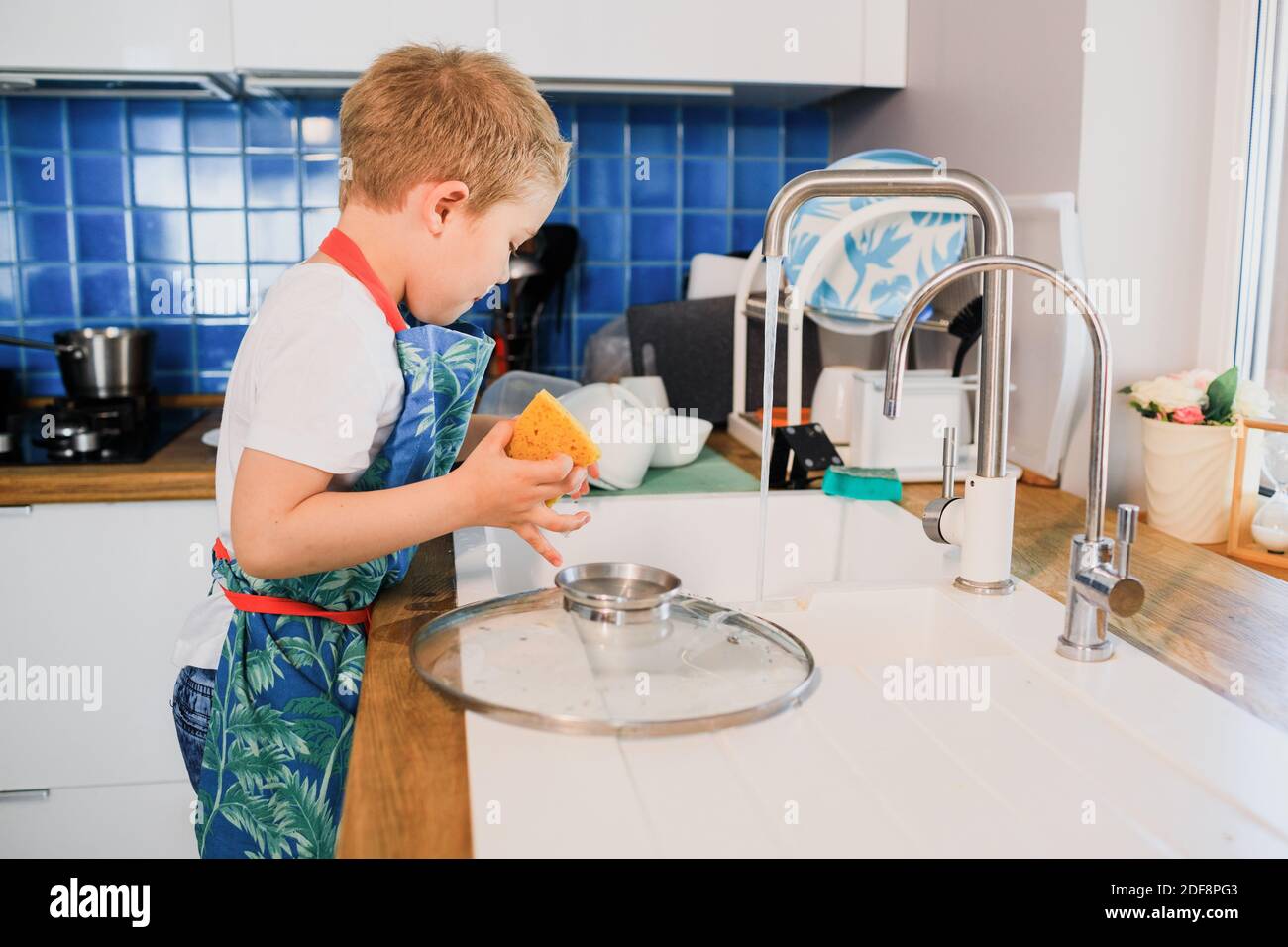 a boy in an apron washes dishes in the kitchen at home Stock Photo - Alamy
