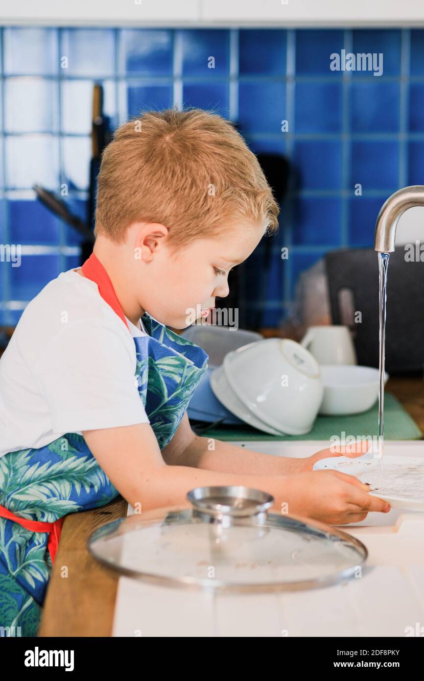 a boy in an apron washes dishes in the kitchen at home Stock Photo - Alamy
