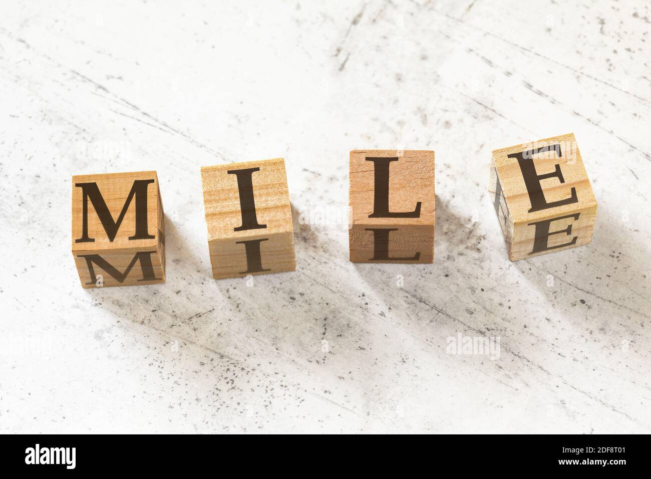 Four wooden cubes with letters MILE (meaning Maximum Impact Little ...