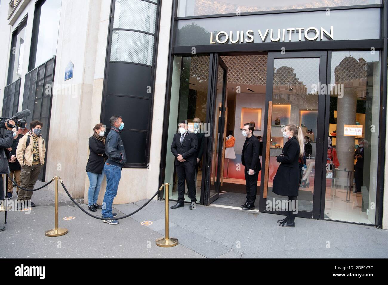 Customers wearing protective face masks queue outside the Louis Vuitton ...
