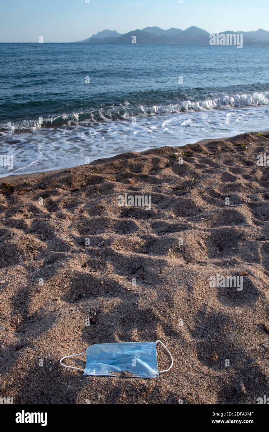 A protective face mask is seen discarded in the sand on a beach in ...