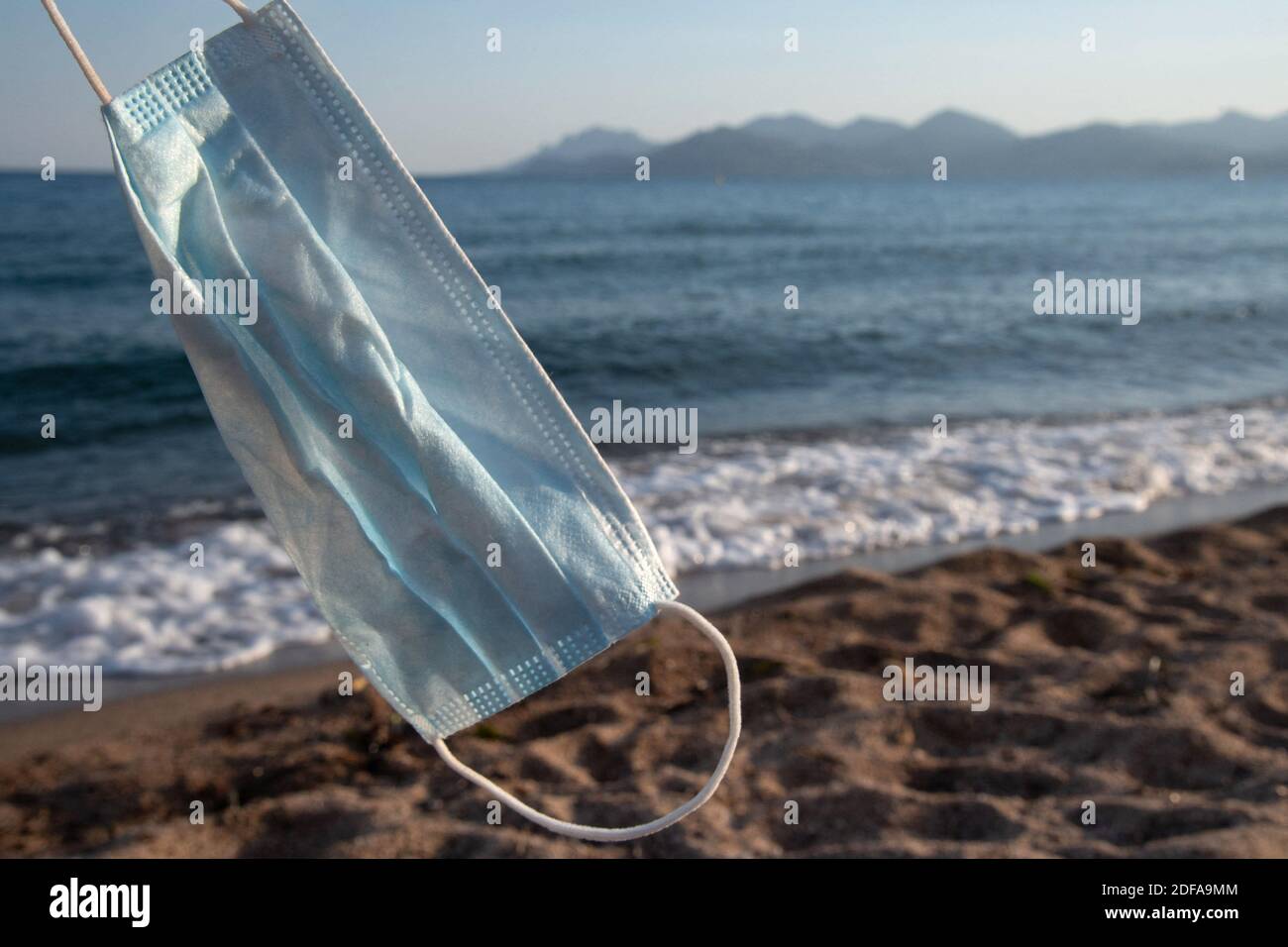A protective face mask is seen discarded in the sand on a beach in ...