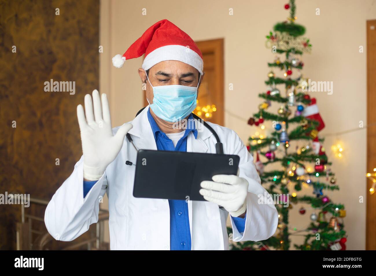Doctor wearing mask santa hat video calling over tablet, christmas ...