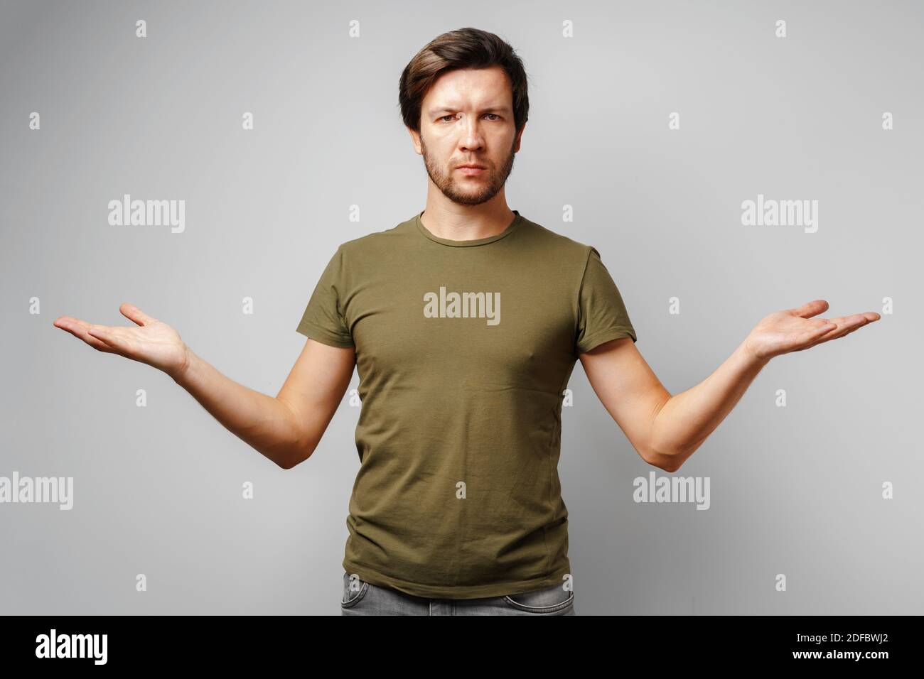 Clueless young man gesturing "i don't know" against grey background ...