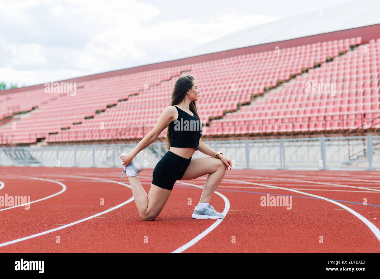 A female coach with dark hair stands on the red running track of the ...